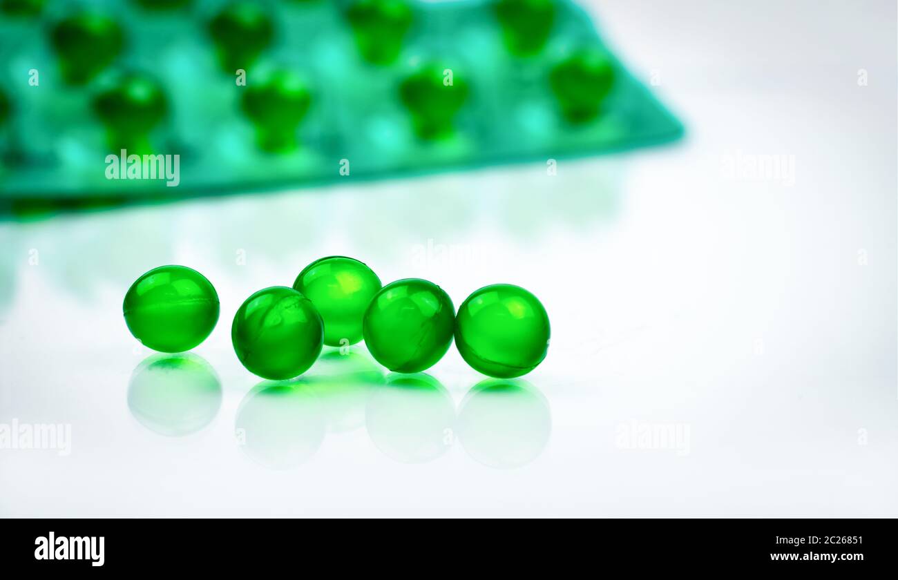 Green round soft capsule pills on blurred background of blister pack ...