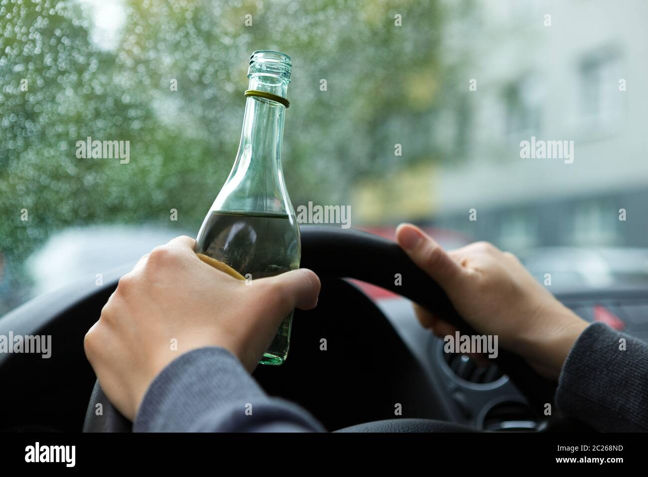 Drunk young driver drinking a bottle of wine during driving the car ...