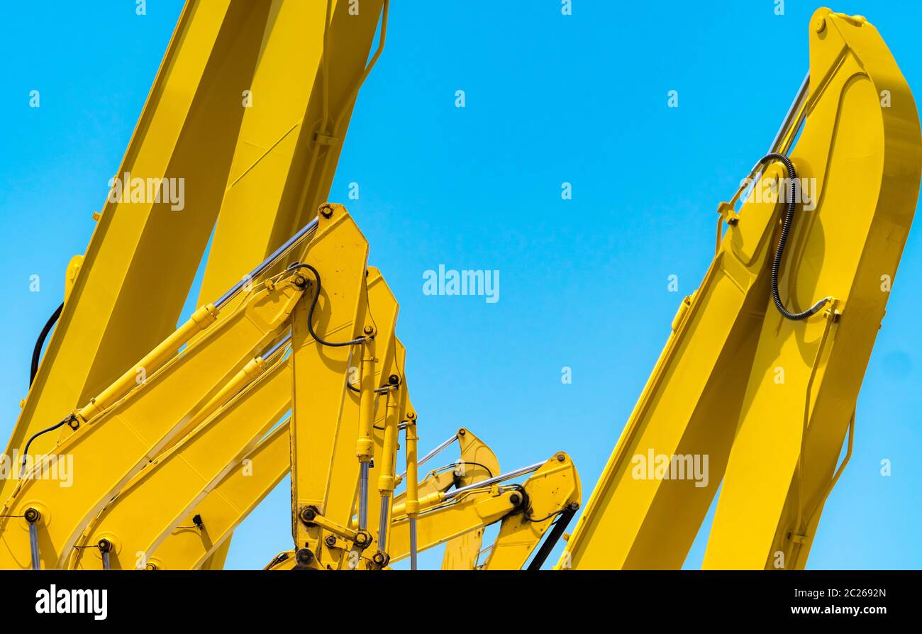 Yellow backhoe with hydraulic piston arm against clear blue sky. Heavy ...
