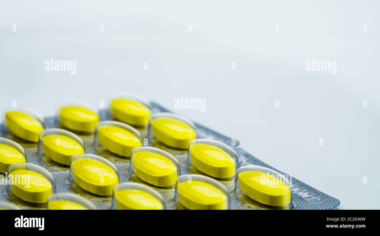 Macro shot detail of yellow oval tablet pills in blister packs on white ...