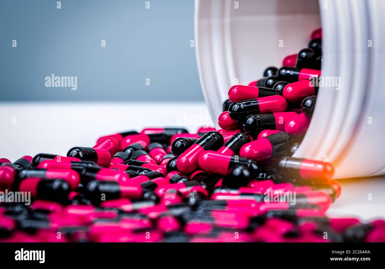 Pink, black capsules pill spilled out from white plastic bottle ...