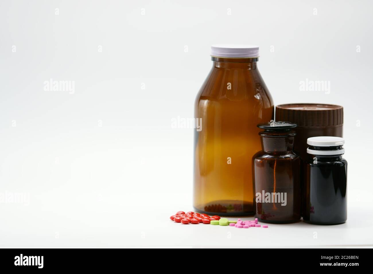 Pink, green, and red tablets on white background with amber drug bottle ...