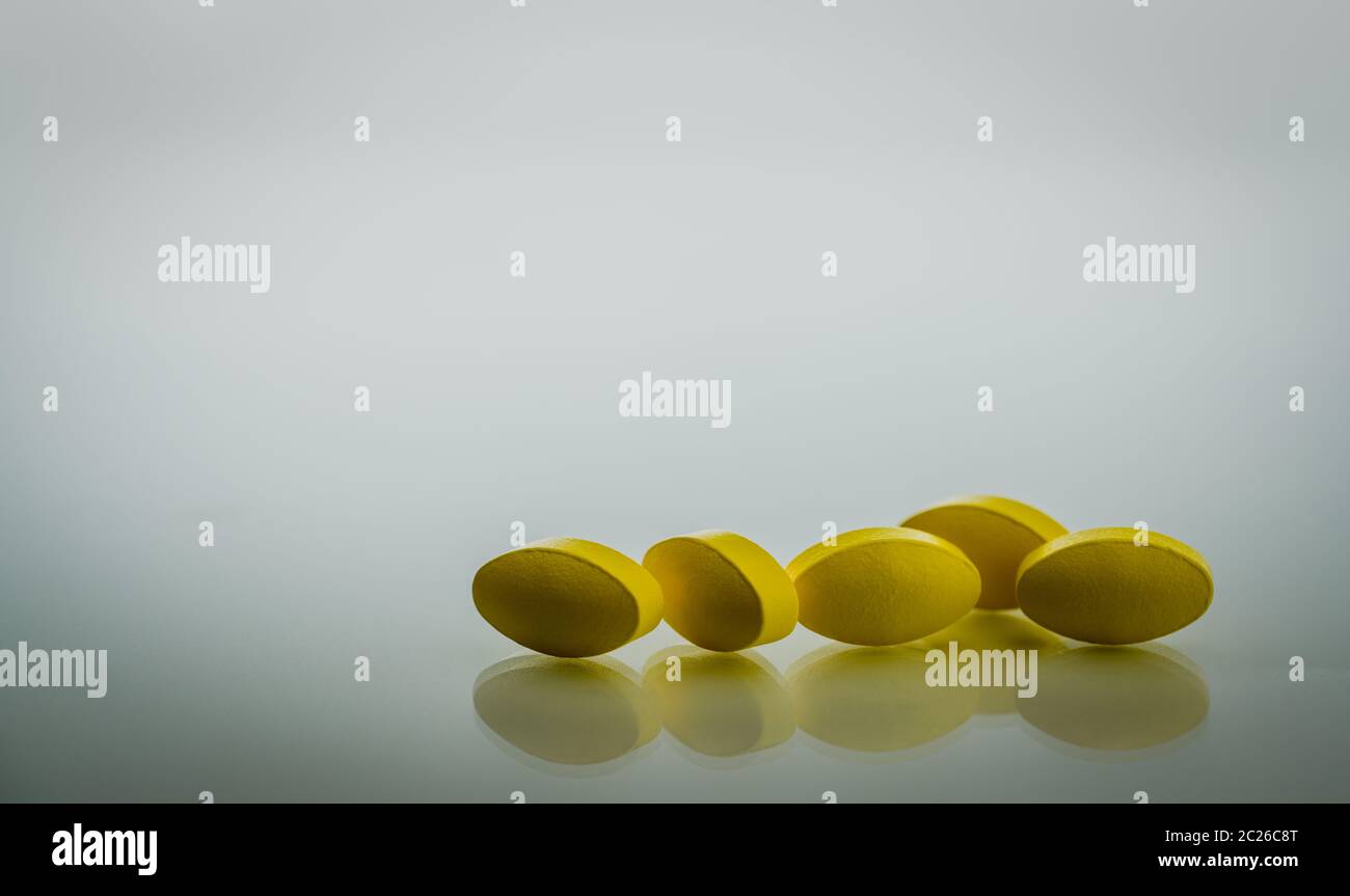Yellow oval tablet pills with shadows on white background with ...
