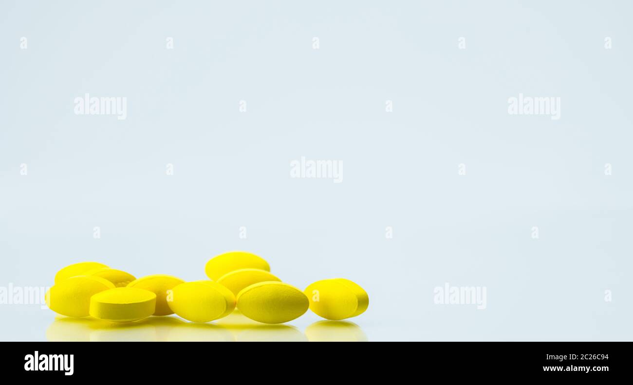 Pile of yellow oval tablet pills on white background with copy space ...