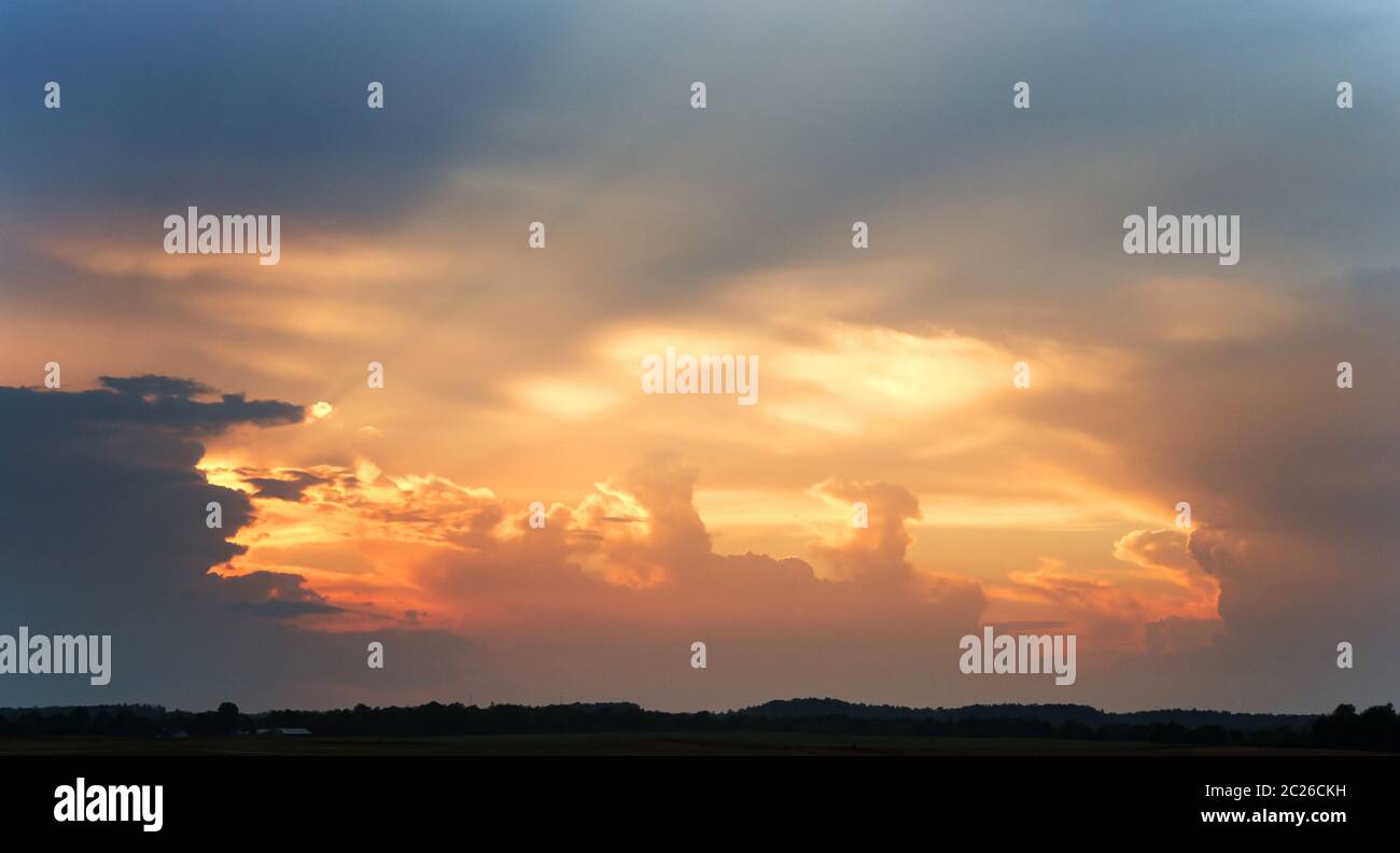 An orange sunset as the sun rays burst through passing storm clouds Stock Photo - Alamy
