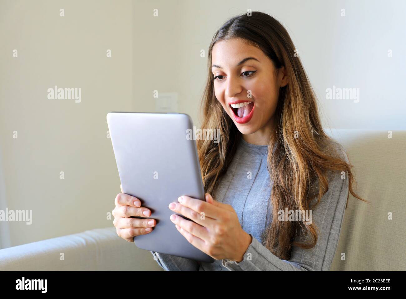 Happy girl using tablet. Excited woman holding tablet pc on sofa at ...