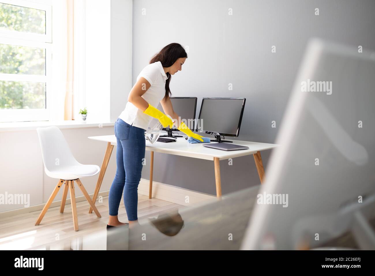 Side View Of Female Janitor Cleaning Desk With Blue Napkin In Office ...