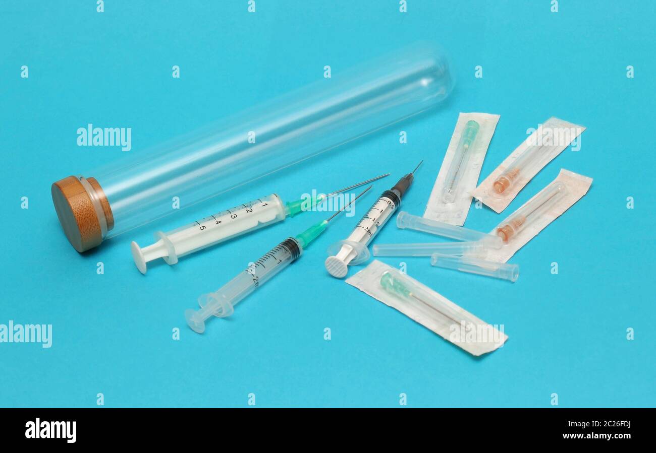 Medical syringes with needles and glass test tube on blue background ...