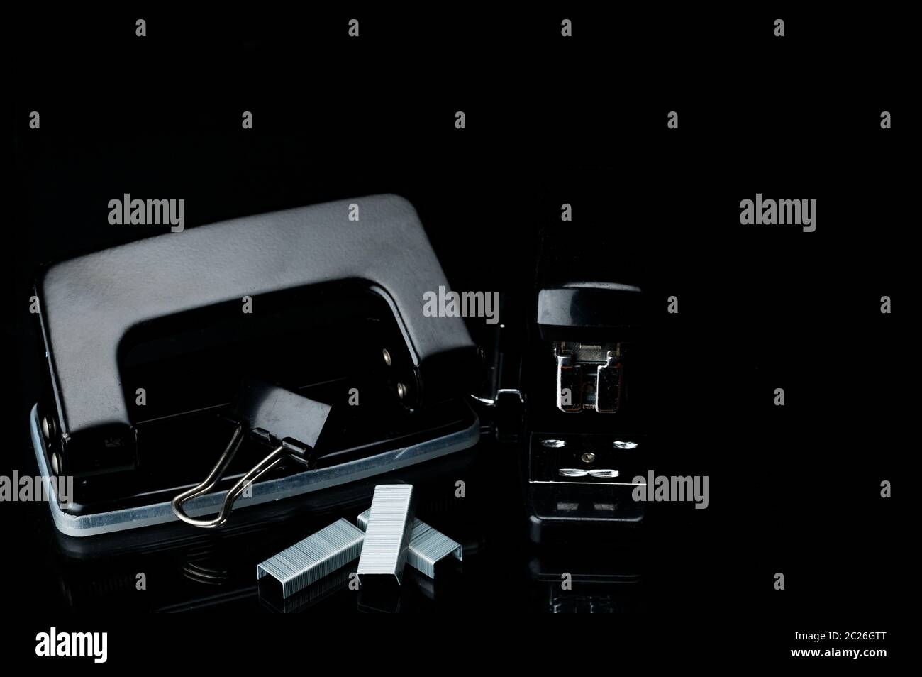 Black stapler, staples, paperclip and punch on dark background with ...