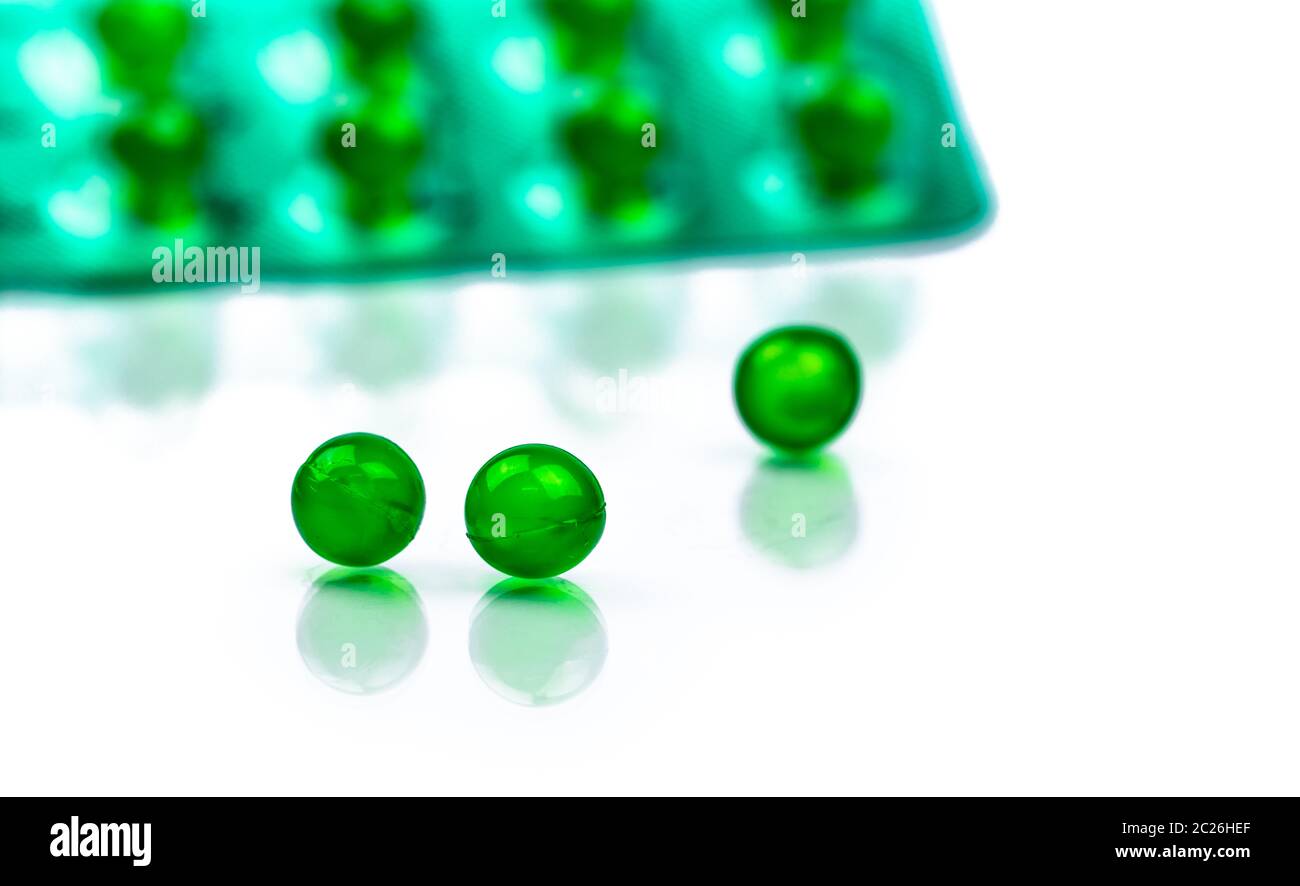 Green round soft capsule pills on blurred background of blister pack ...