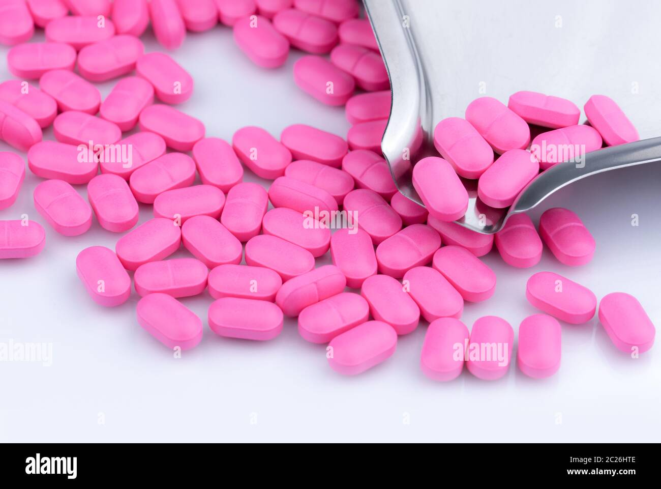 Pile of pink tablets pill on white background near stainless steel drug ...