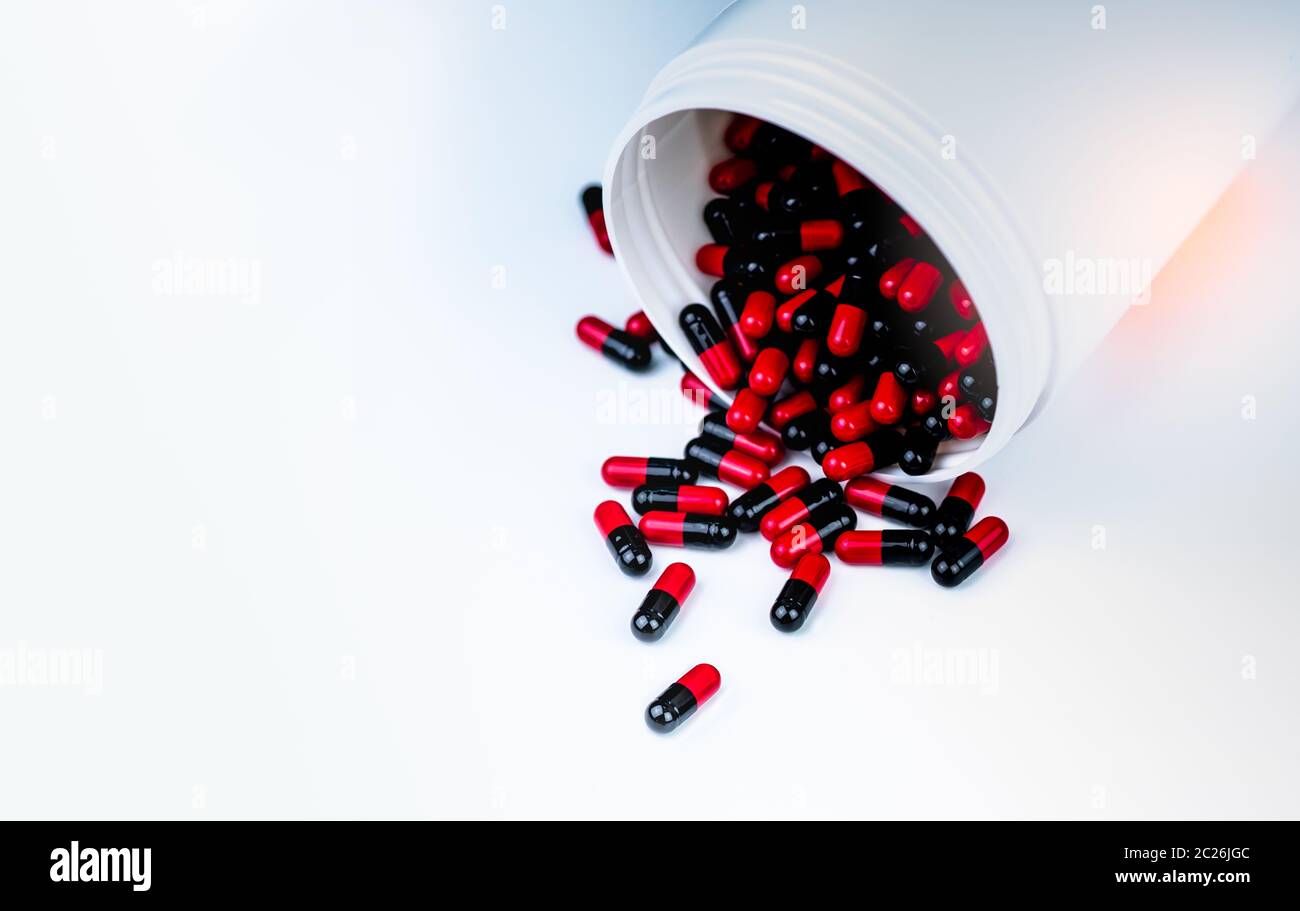 Red, black capsules pill spilled out from white plastic bottle ...