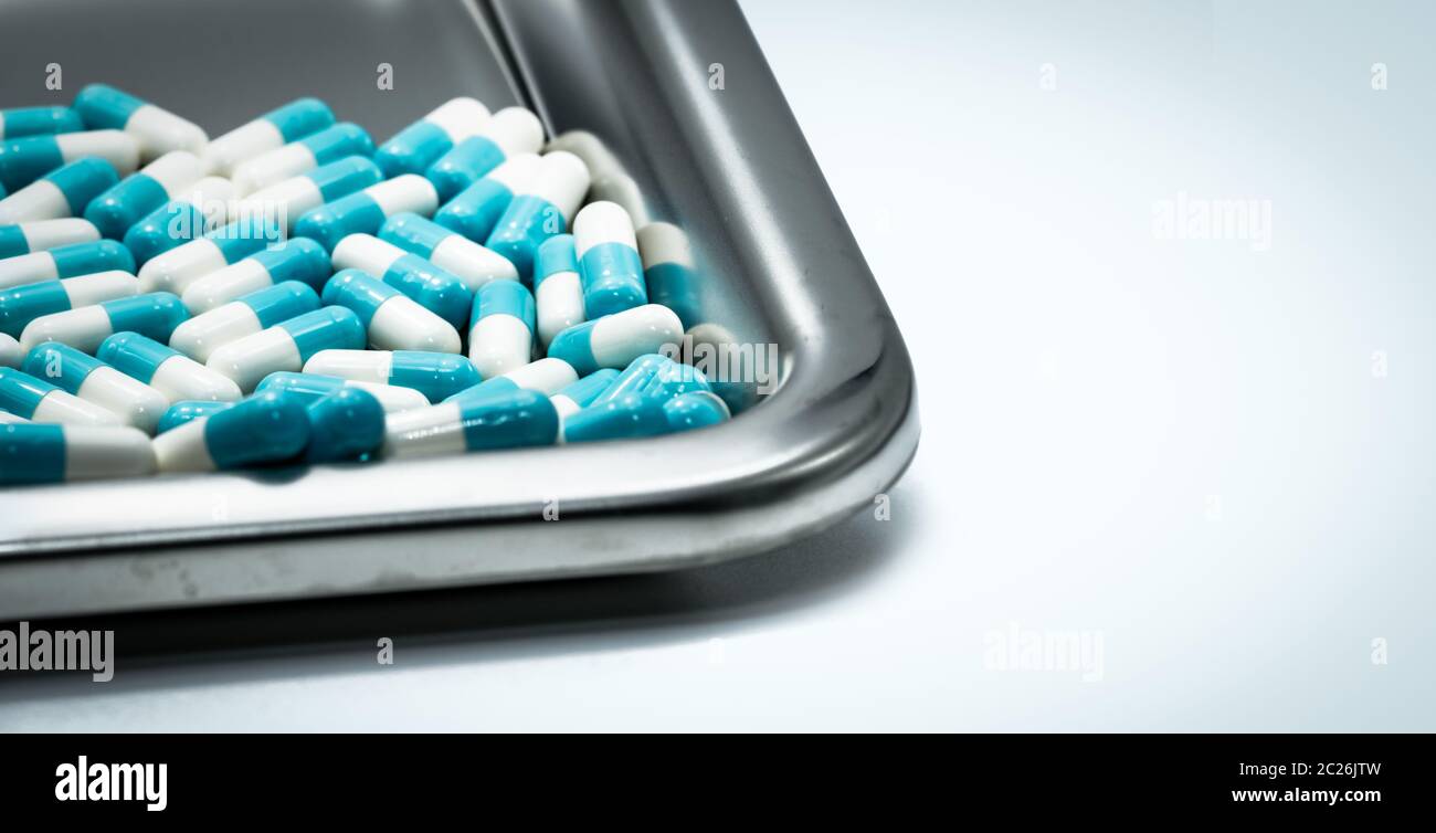 Blue-white capsule pills on stainless steel drug tray. Pharmaceutical ...