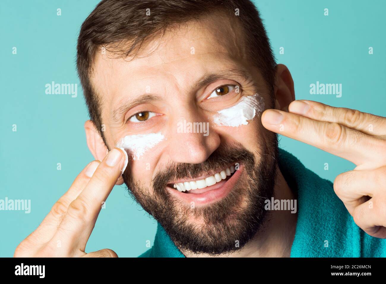 The smiling cheerful handsome man is applying face cream for men on his ...