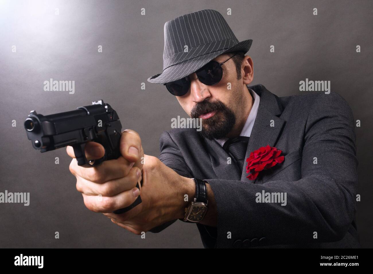 The gangster in elegant suit and hat in vintage style is aiming with ...