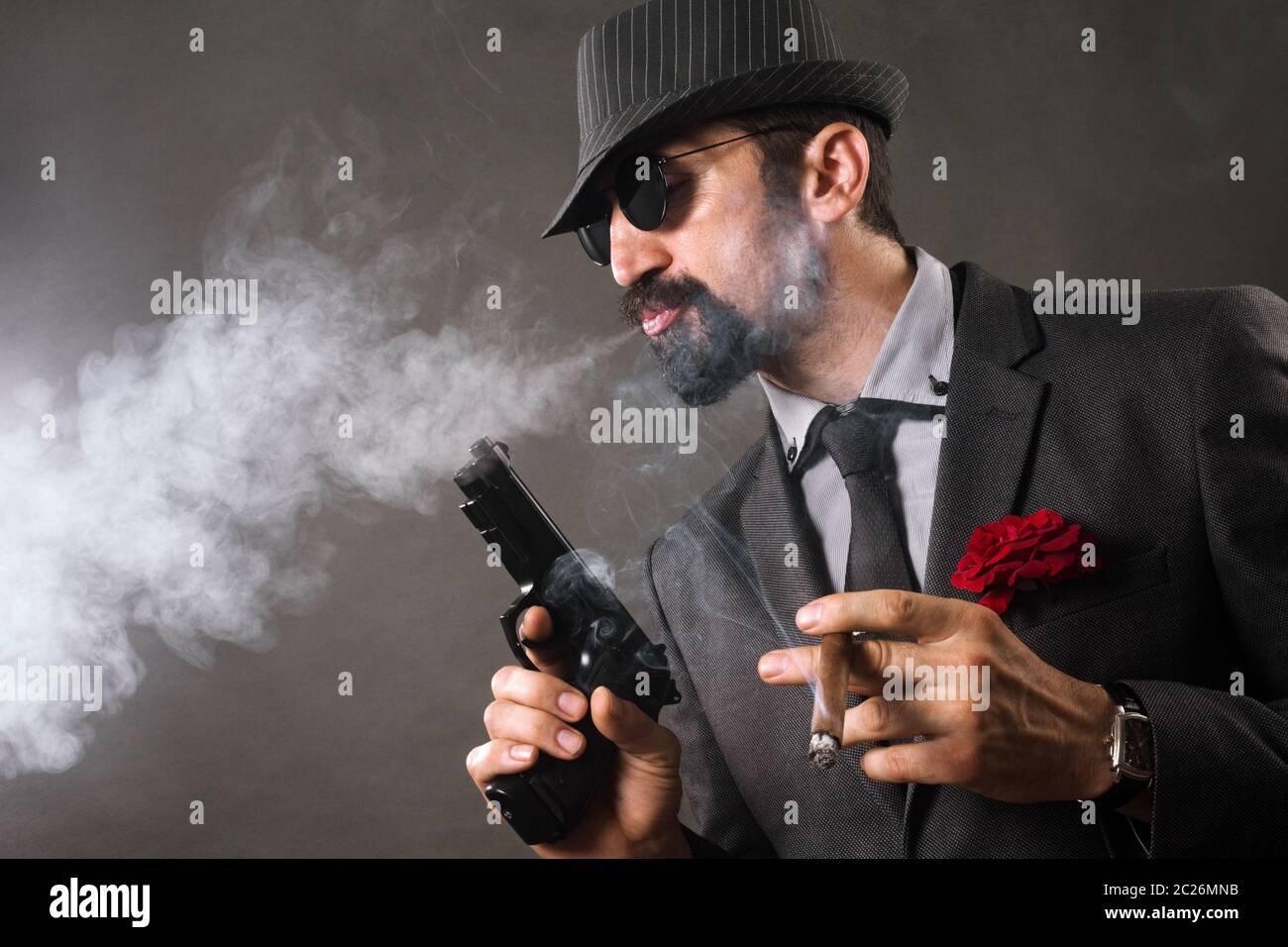 The elegant mafia boss or gangster is smoking cigar and holding pistol ...