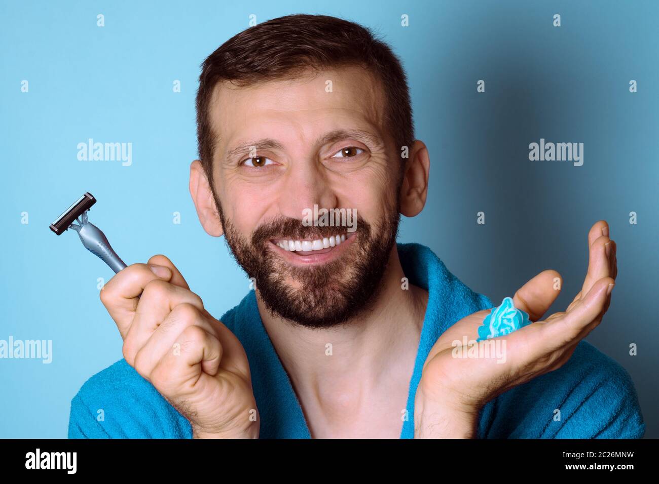 The smiling bearded man is ready for shaving and holding a razor and ...