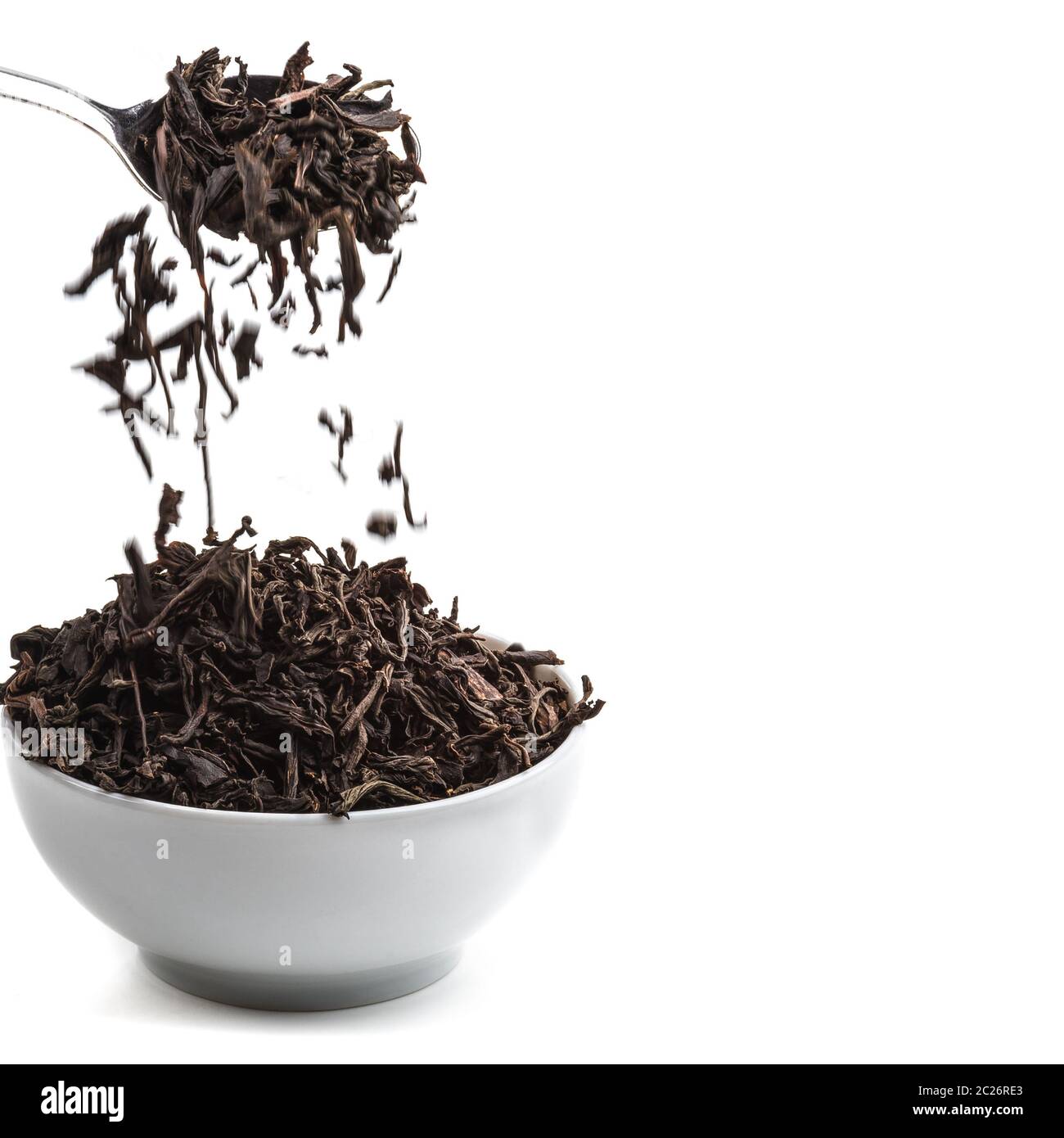 Dried tea pour from the spoon in ceramic cup over white background ...