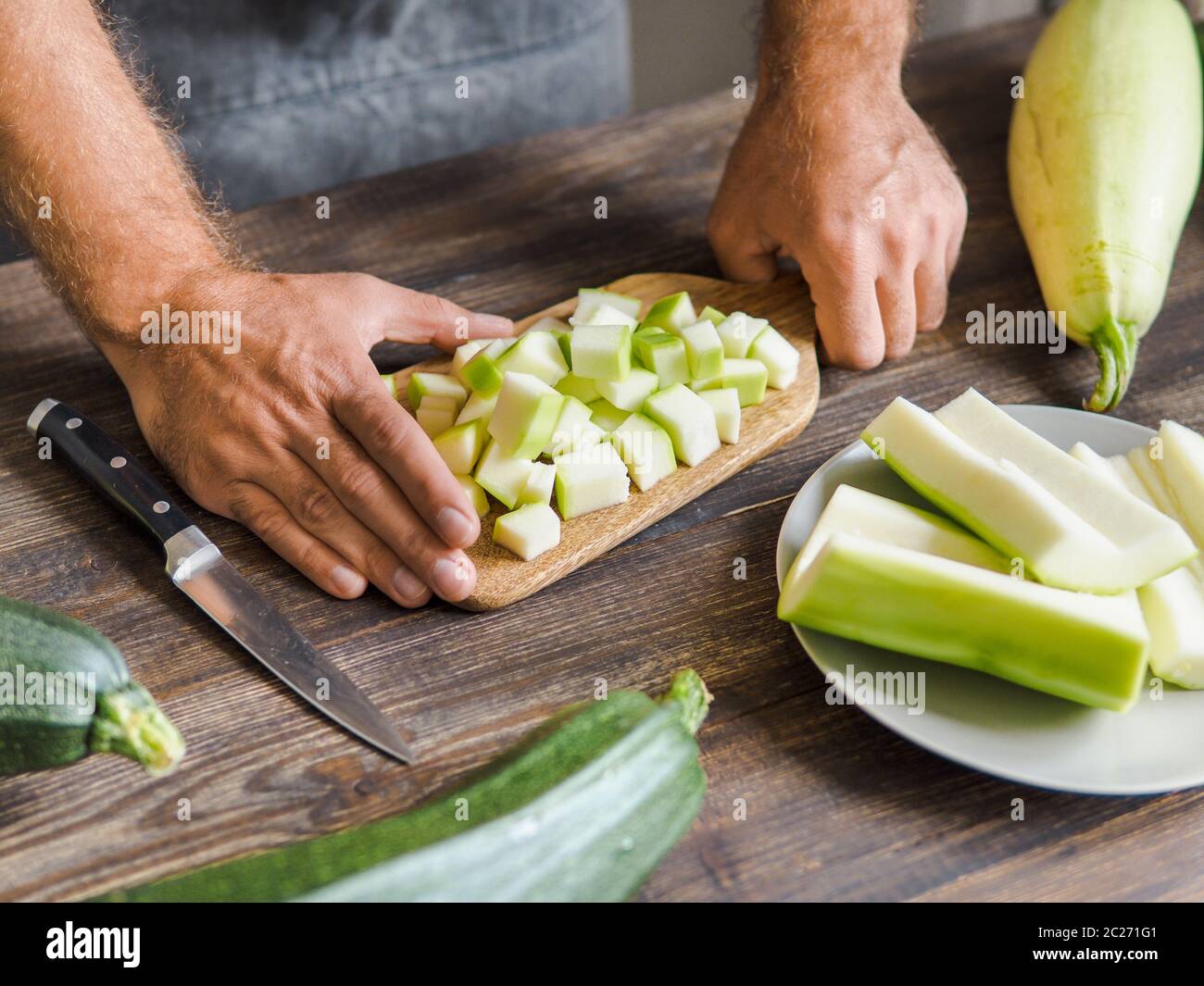 Zucchini harvest. Man slices zucchini cubes for freezing on wooden ...