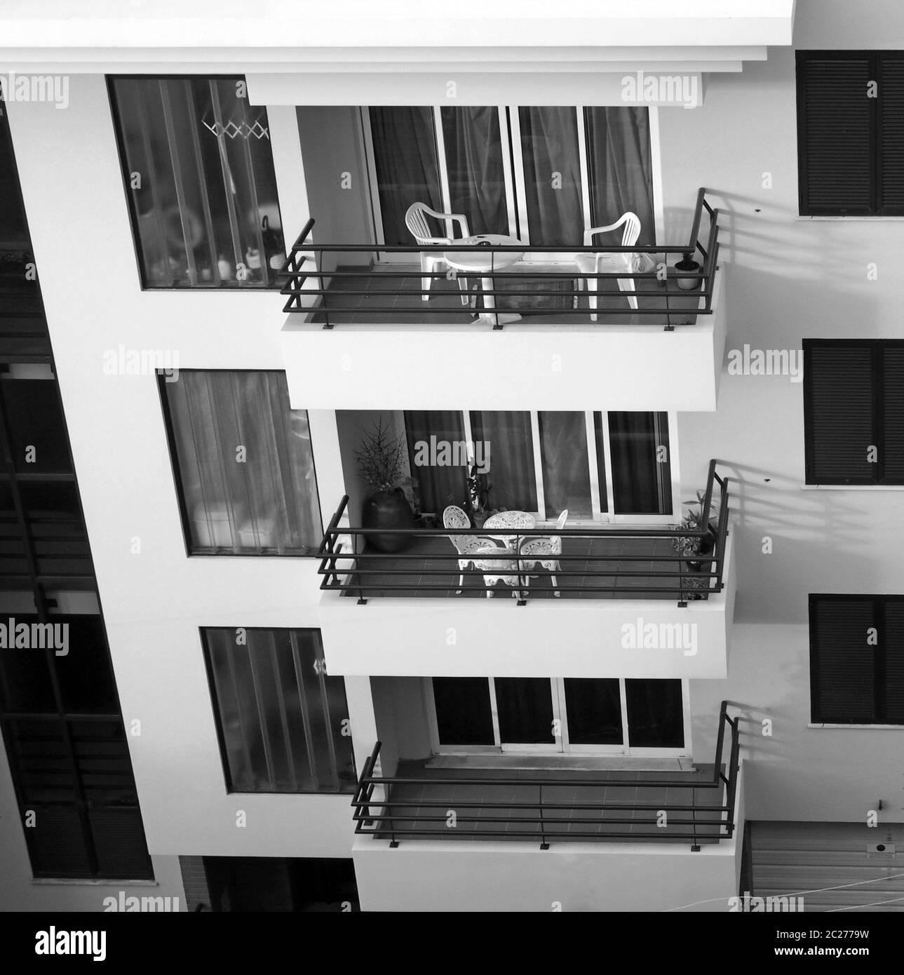 monochrome image looking down on a row of balconies with tables and ...