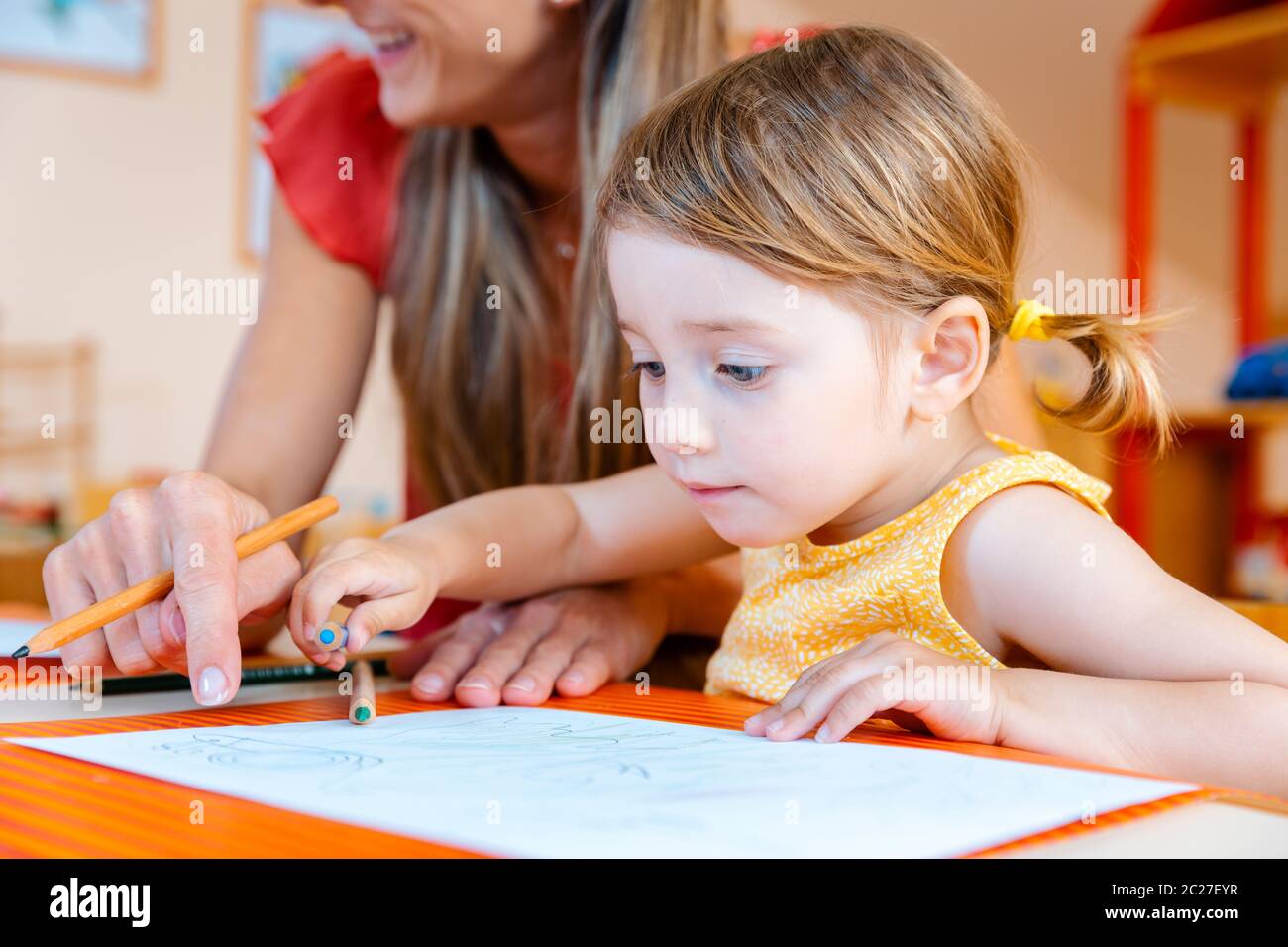 Children drawing with pencils in play school, the teacher helps Stock ...