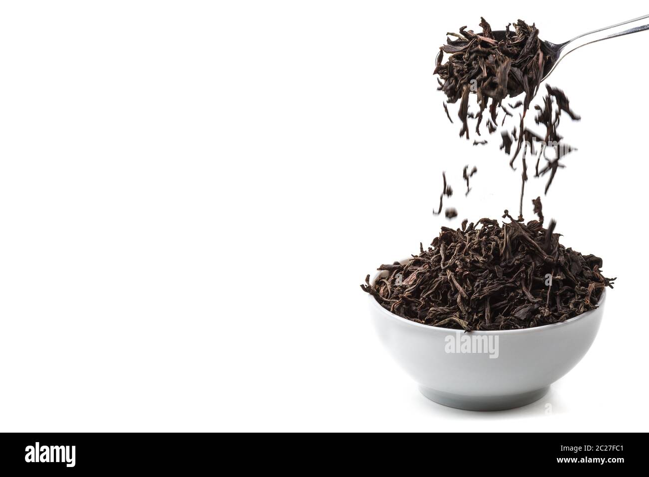 Dried tea pour from the spoon in ceramic cup over white background ...