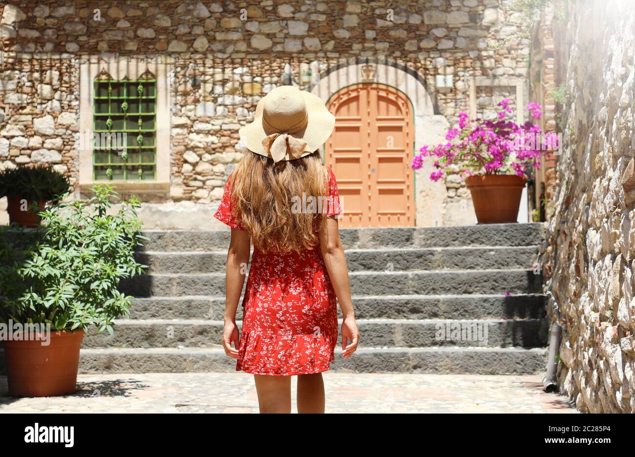 Curious young woman with red dress and hat walking in street in ...