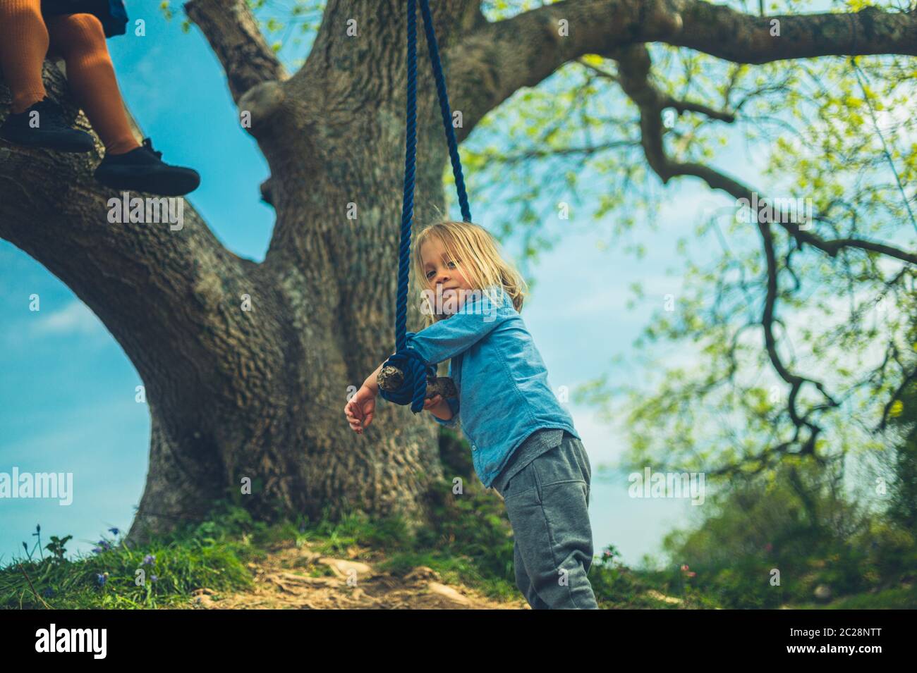 A little preschooler is resting on a rope swing with his mother sitting ...