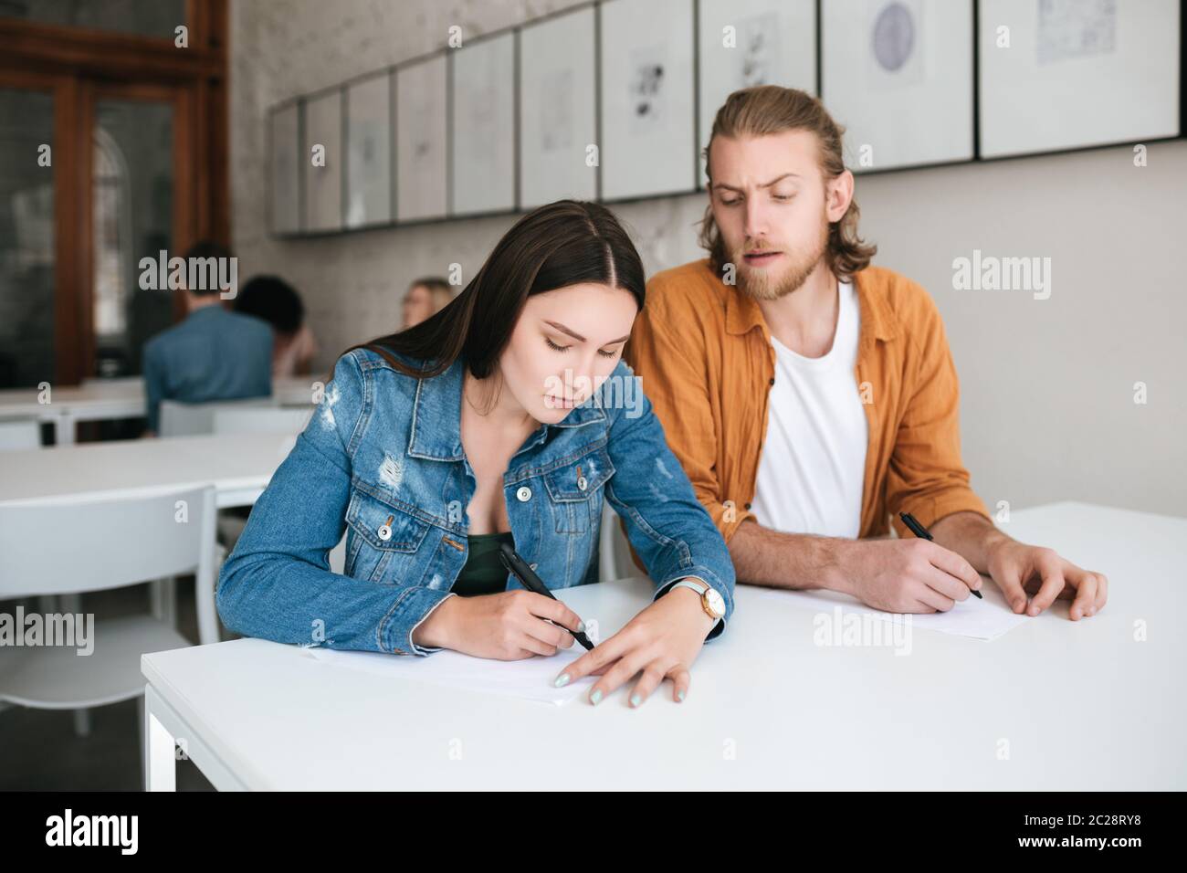 Young man peeping into test of his classmate while sitting in classroom ...