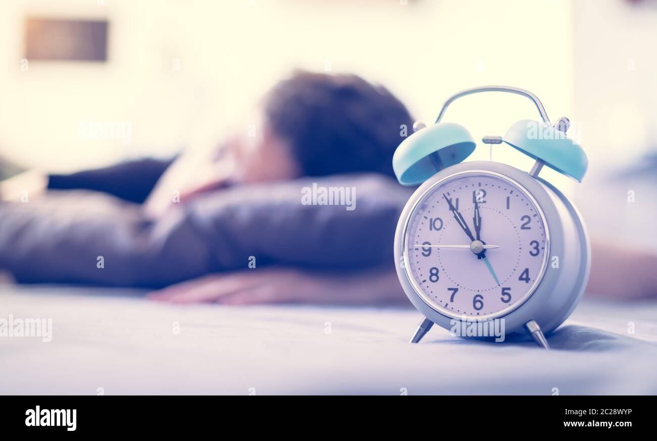 Alarm clock in the morning. Young man sleeps in the blurry background ...