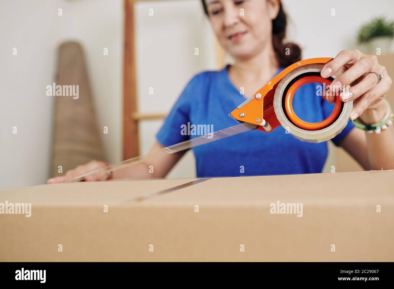 Asian woman wearing blue T-shirt closing box full of household things ...