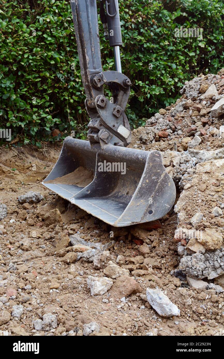Excavating a concrete driveway alongside a hedge; metal digger bucket ...