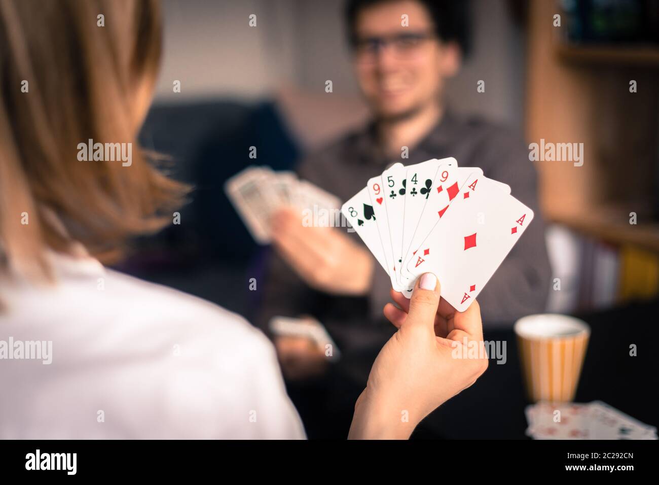 Friends are playing cards together at home. Woman is holding cards in ...
