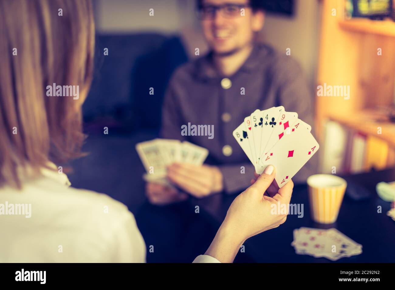 Friends are playing cards together at home. Woman is holding cards in ...