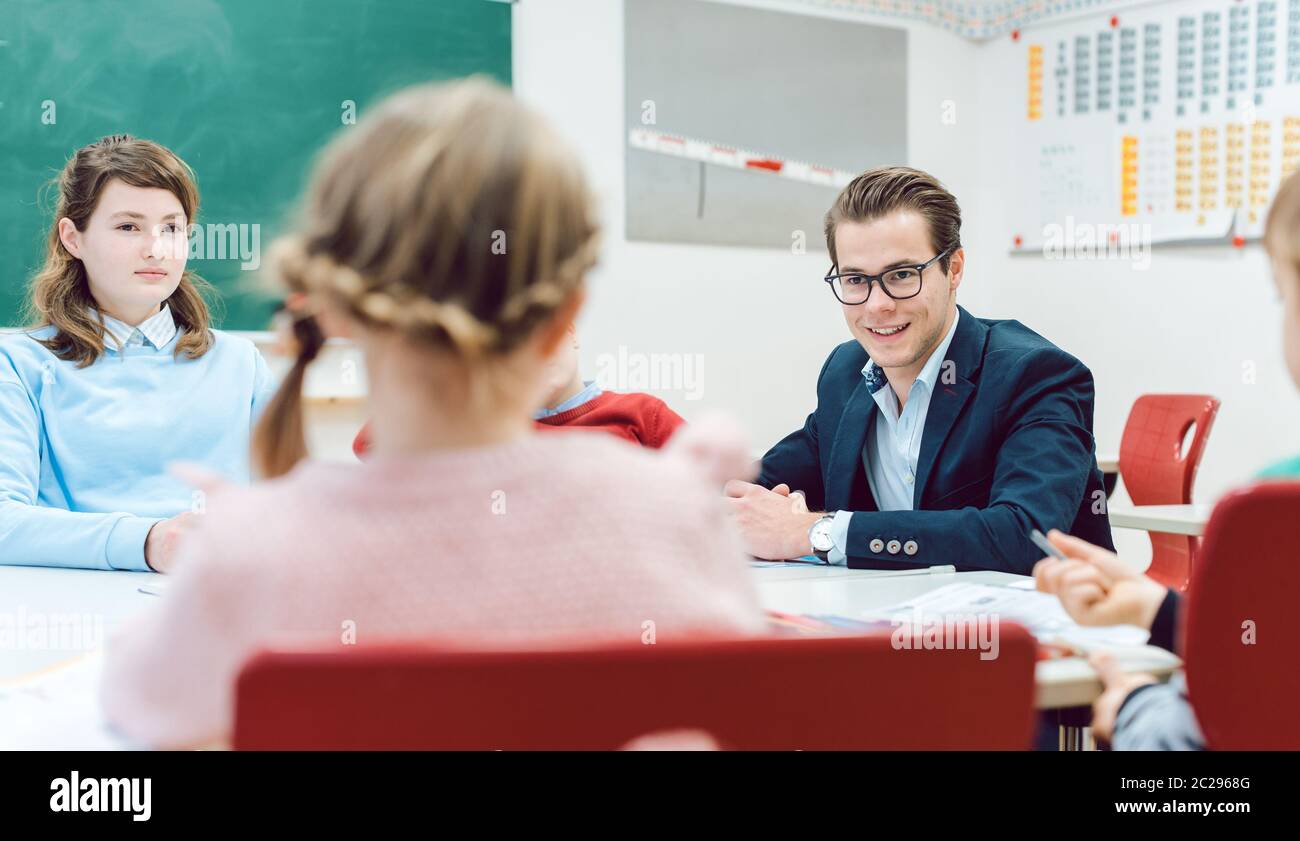 Pupils and teacher cooperating in teamwork exercise sitting around a ...