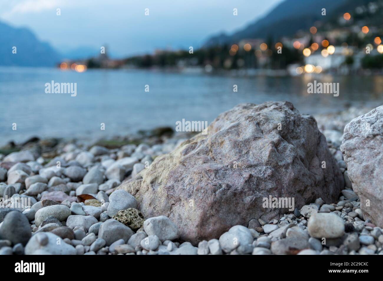 Heavy rock on the beach, blurry background with lake and village ...