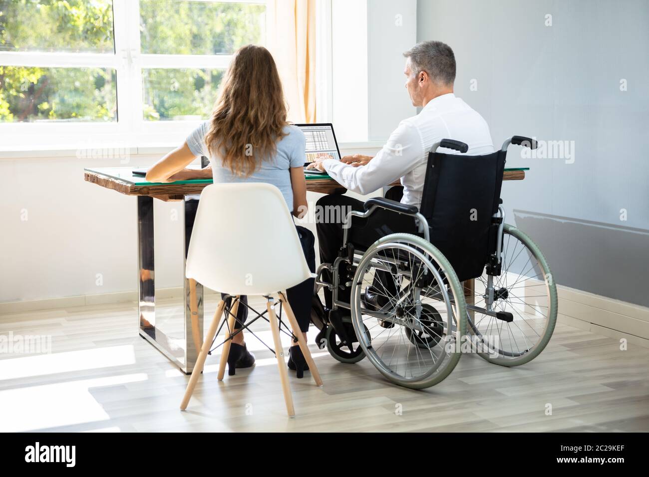 Disabled Businessman Sitting With His Partner With Laptop Over Desk In ...