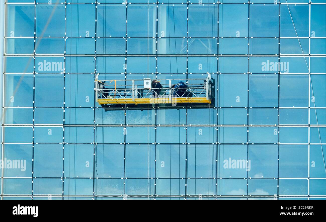 Worker inspecting glass window installation of tall glass exterior ...