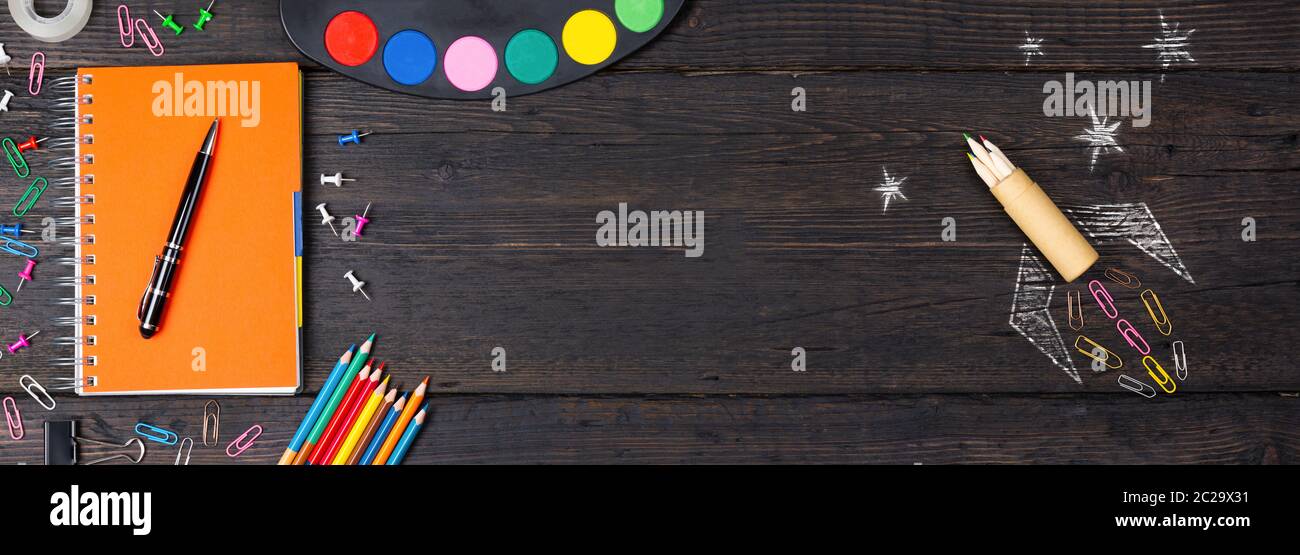 School stationery supplies and hand drawn rocket ship on dark ...