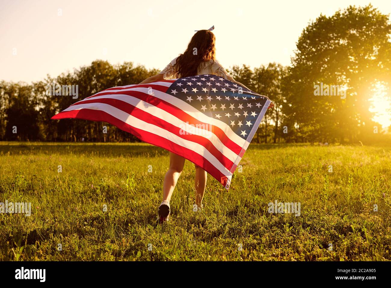 Back view of young woman with American flag running towards sunset in ...