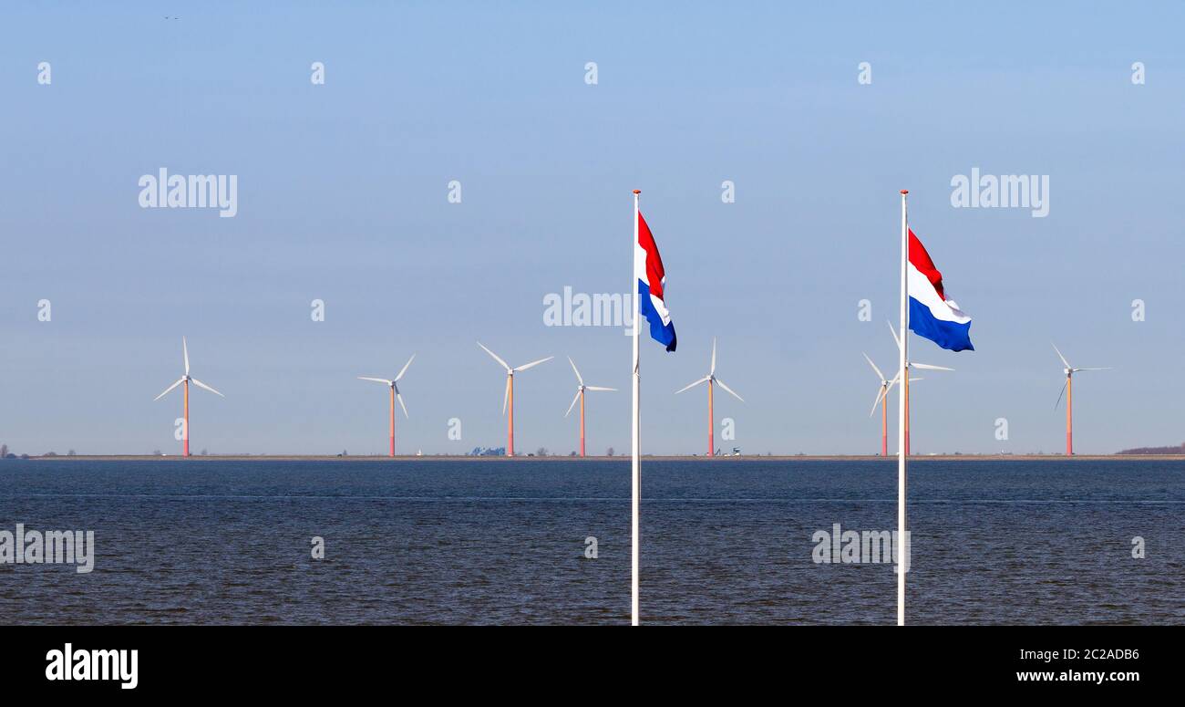 Dutch flag waving at the shore of the Markermeer lake with windmills ...