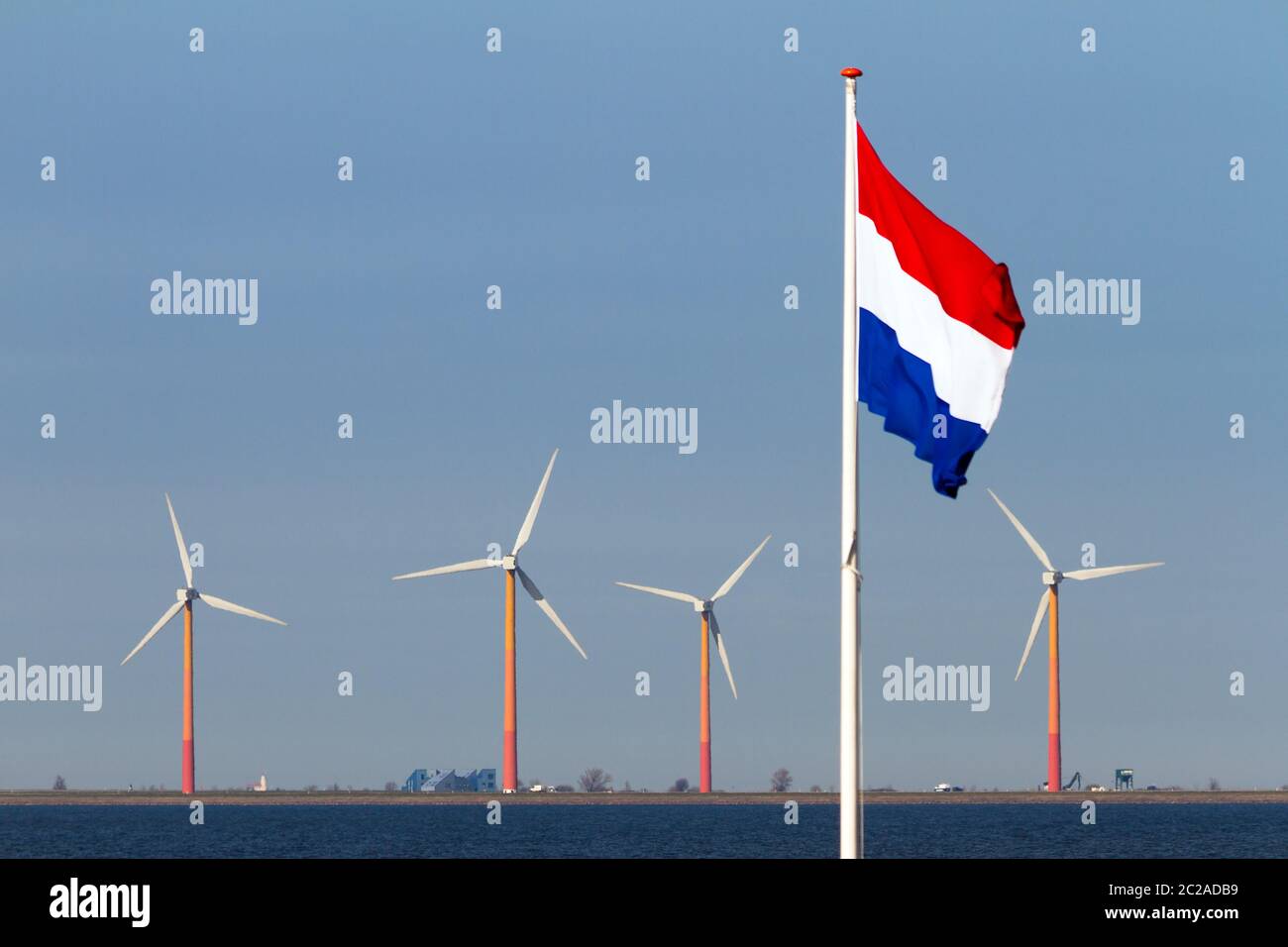 Dutch flag waving at the shore of the Markermeer lake with windmills ...
