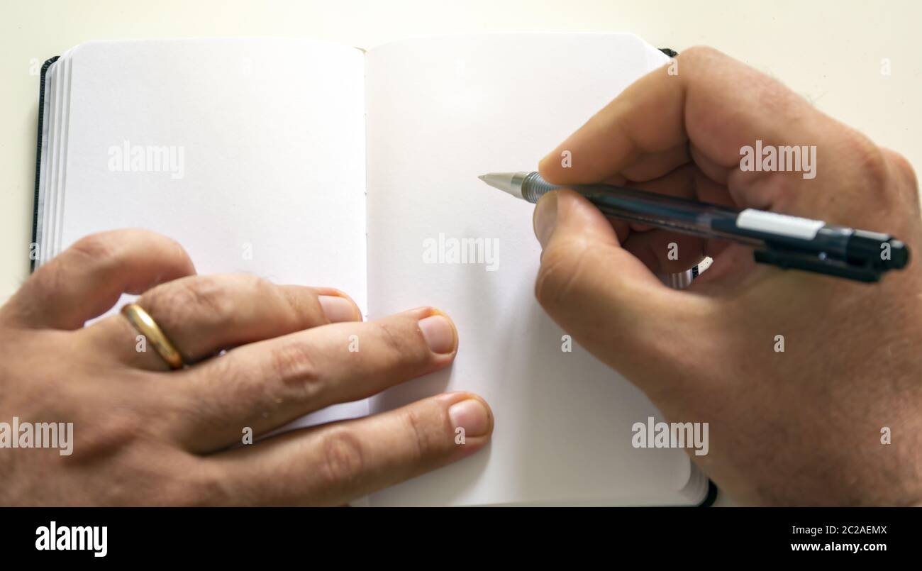 male hands holding a ballpoint pen to write on the blank pages of an ...