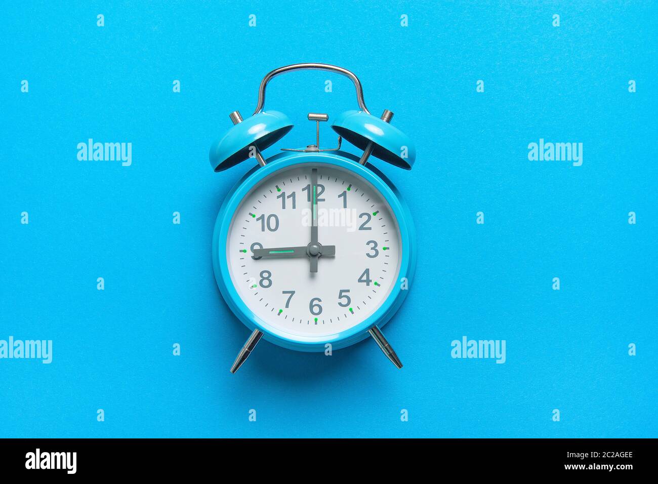 Blue vintage alarm clock at nine o’ clock lying on a blue background ...