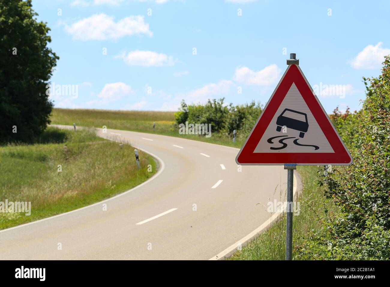 Slippery road - Road sign stands on a sharp turn Stock Photo - Alamy