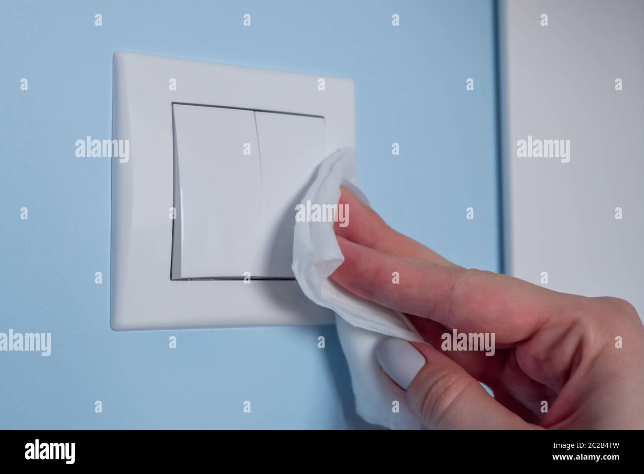 Woman hands cleaning white light switch on blue wall with antiseptic ...