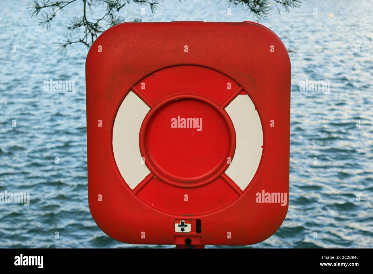 Red lifebelt in housing box on the edge of a lake with overhanging ...
