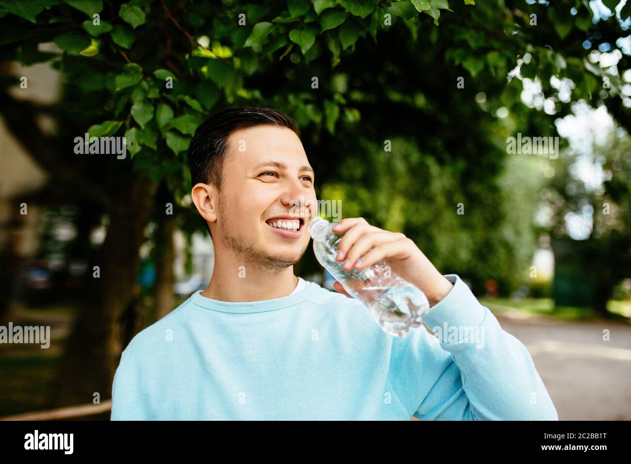 Young smiling man drinks water from bottle in summer day Stock Photo ...