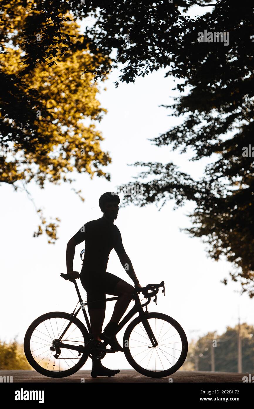 Strong man in silhouette wearing cycling clothes and helmet, posing on ...