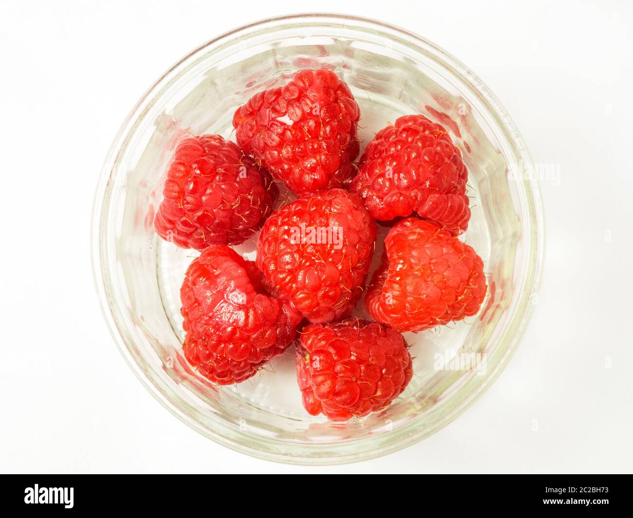 A glass ramekin dish of fresh raspeberries centred on a white ...